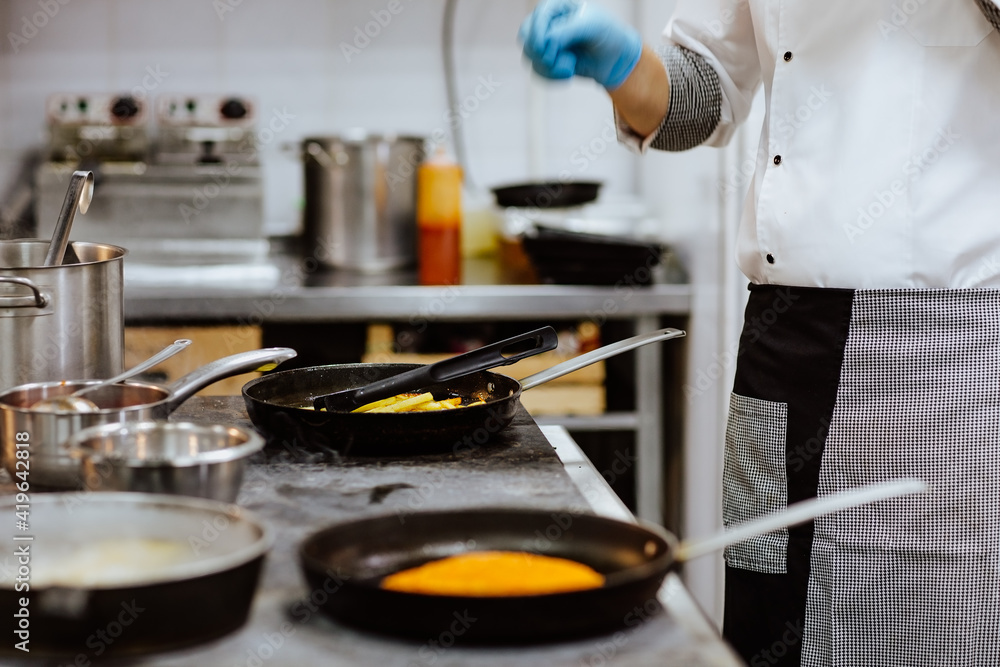 Cook in uniform frying potato in skillet on the restaurant's kitchen ...