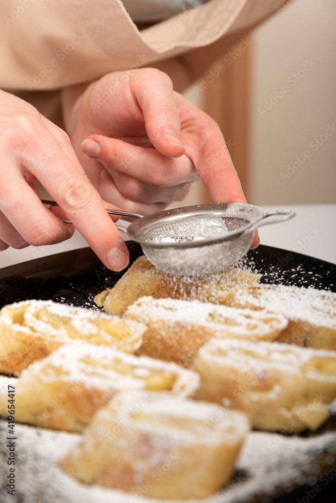 Chef sprinkles icing sugar on the apple roll. Strudel feed. Vertical ...