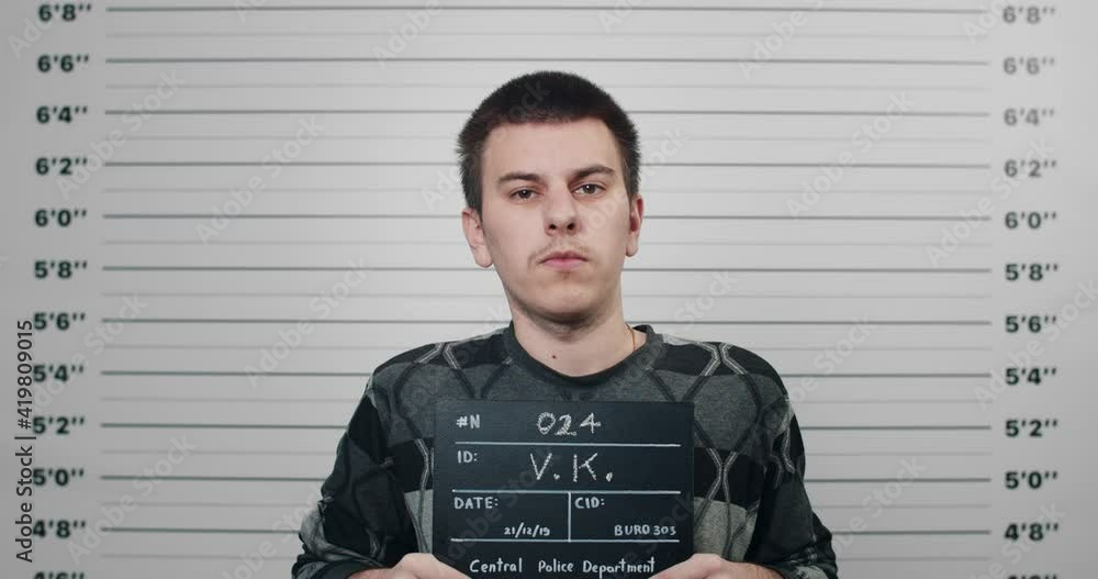 Portrait of male criminal holding sign for photo in police department ...