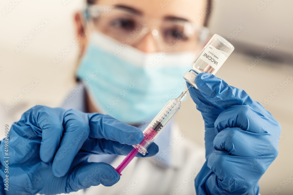 Female medical employee takes a dose of vaccine into syringe during ...