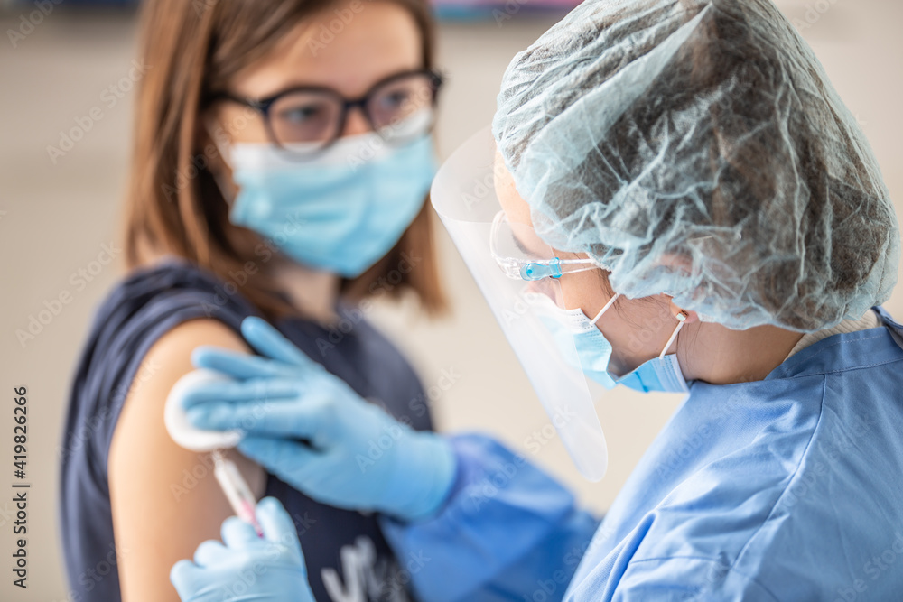 Helathcare employee wearing gloves, protective shield and a cap applies ...