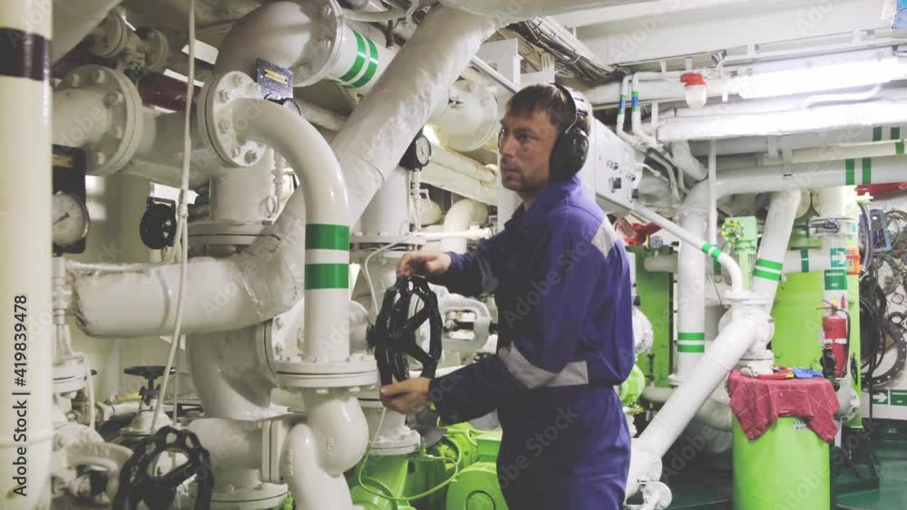 concentrated motor mechanic rotates black valve standing in engine room ...