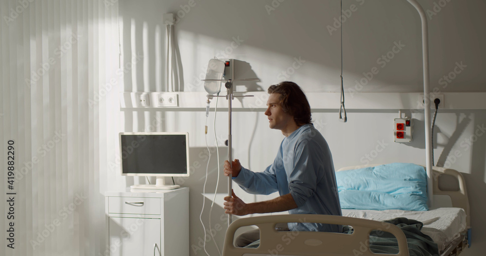 Portrait of male patient standing up holding stand with saline drip bag ...