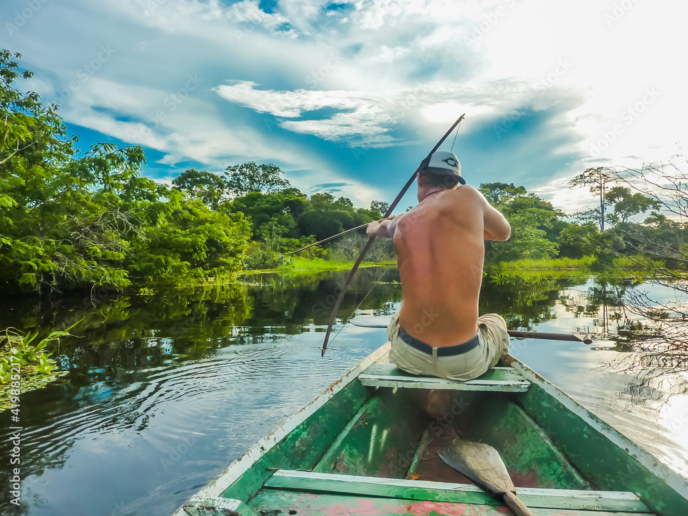 A young man bow hunting for Piranhas, in the middle of the Amazon rain ...