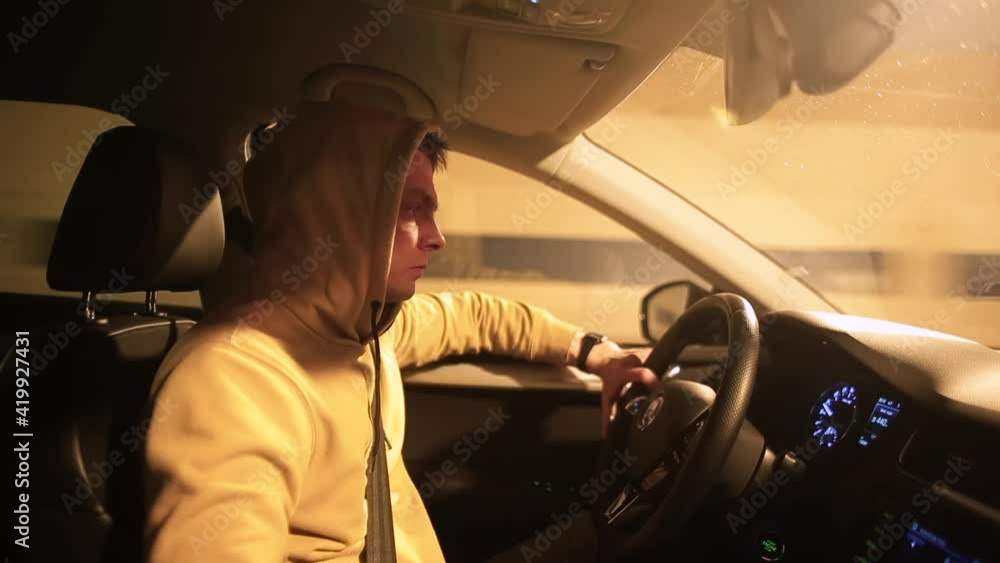A man in a hood is hiding from the police in a night city. He looks in ...