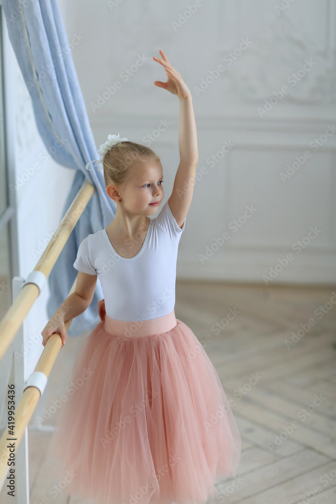 A cute ballerina girl in a full skirt and pointe shoes standing near a ...