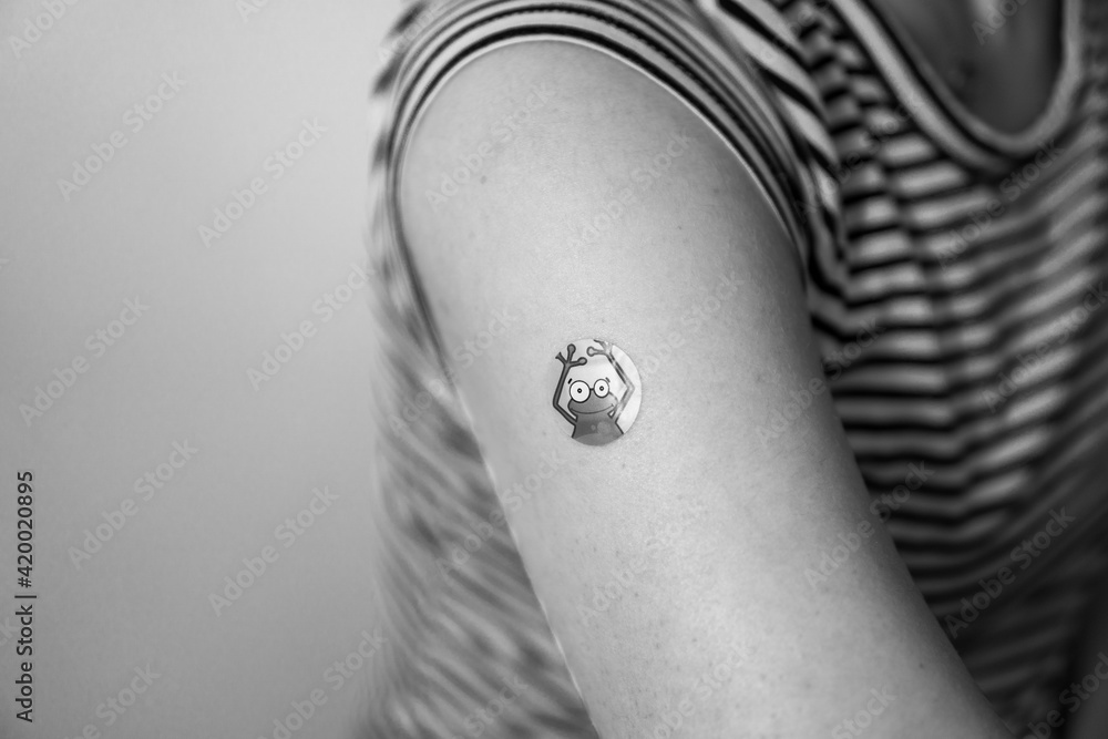 An arm of a woman with a fun adhesive bandage after vaccine injection ...