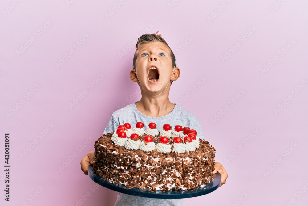 Adorable caucasian kid celebrating birthday with cake angry and mad ...