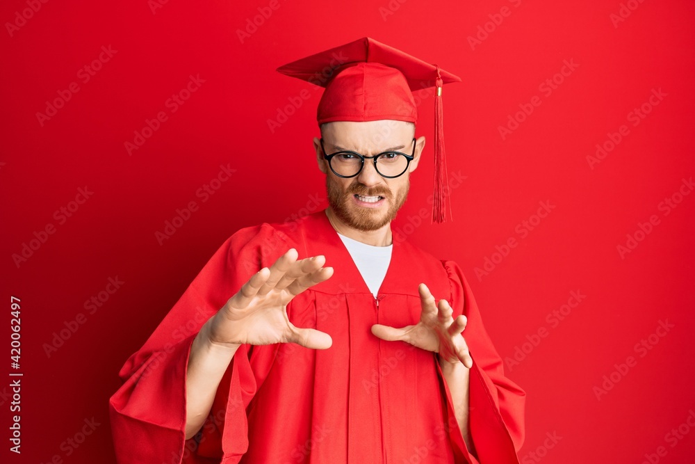 Young redhead man wearing red graduation cap and ceremony robe ...