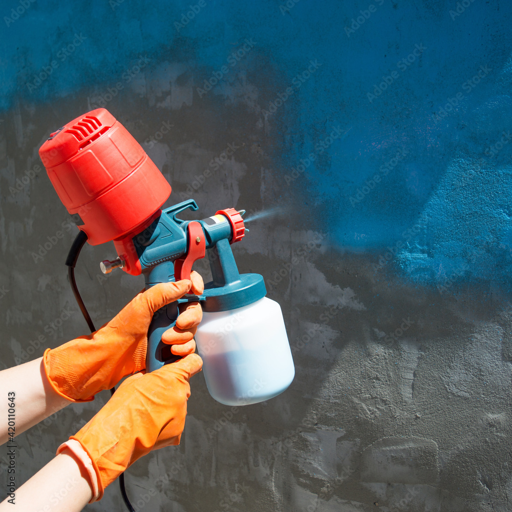 The worker's hands in orange gloves hold a hand-held spray gun ...
