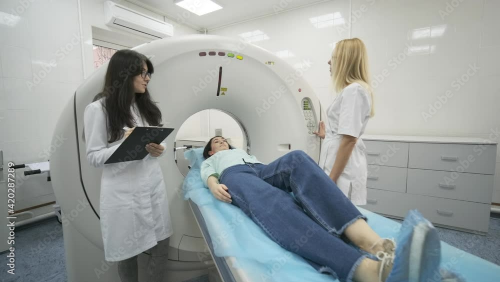 Female patient is undergoing CT or MRI scan under supervision of two ...