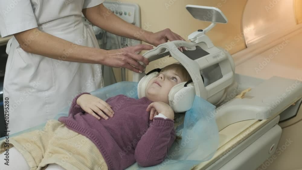 Doctor radiologist puts coil on the head of the patient little girl to ...