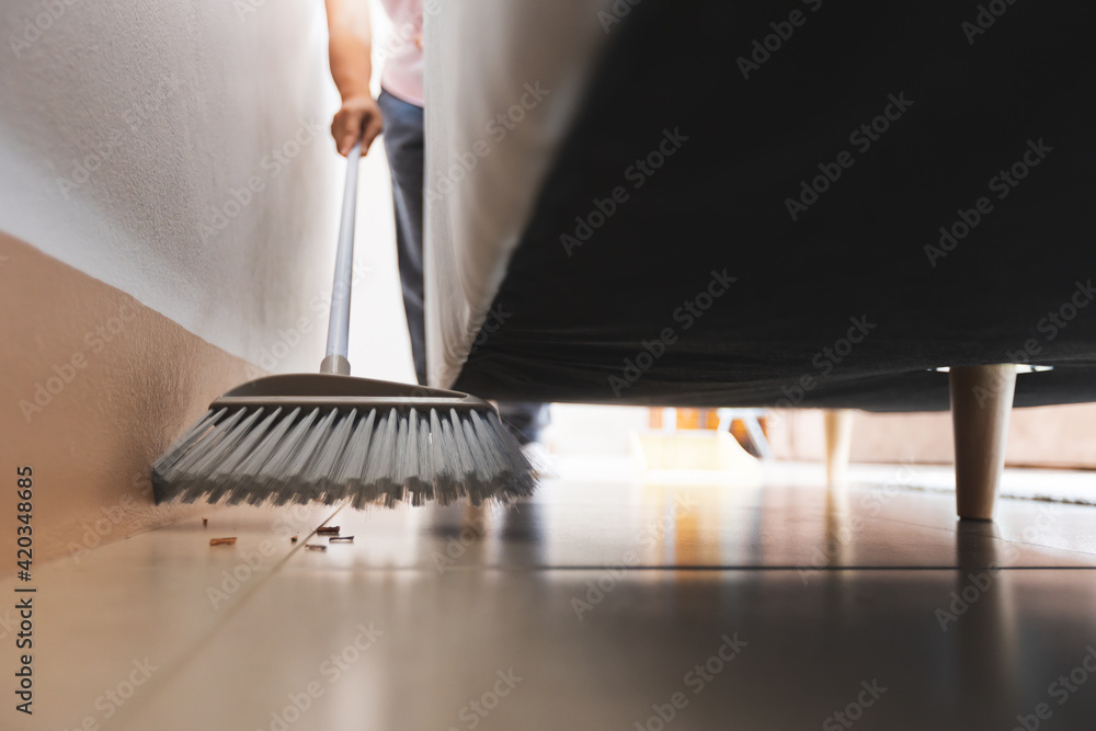 Asian woman cleaning and sweeping dust the floor under the sofa with a ...