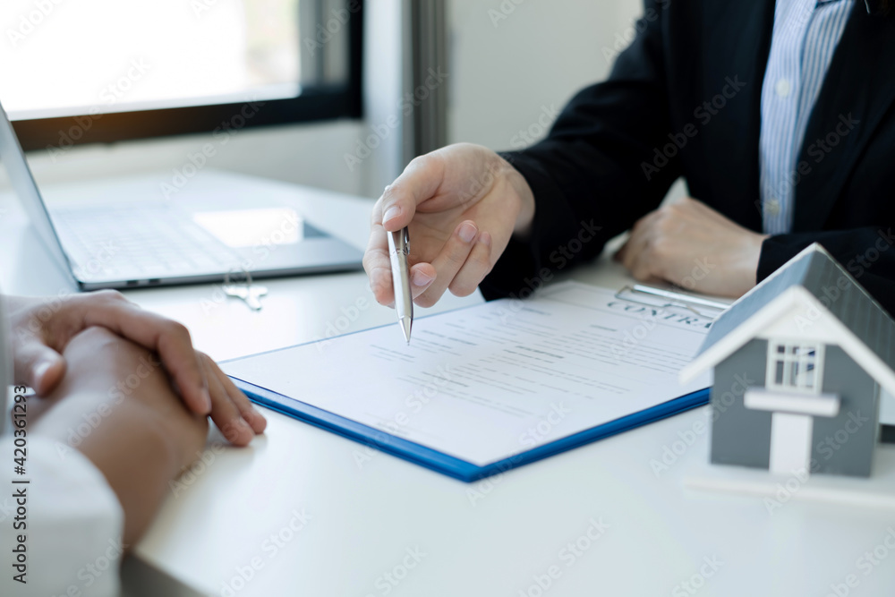 A real estate agent with a House model is talking to clients about ...