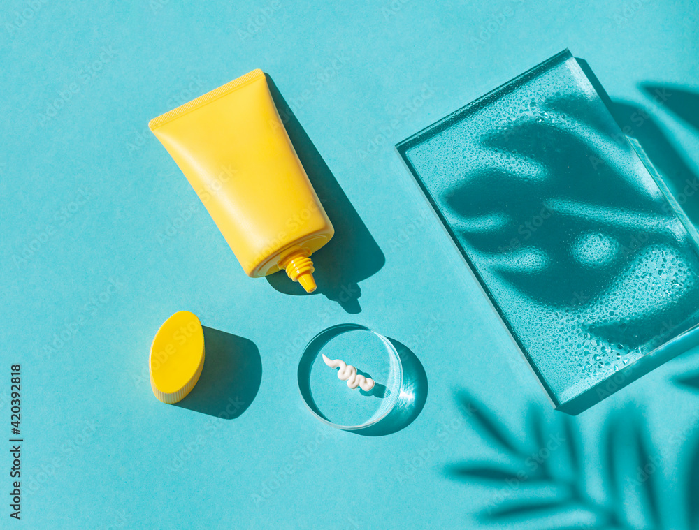Sun cream yellow tube on the blue wet background with tropical leaves ...