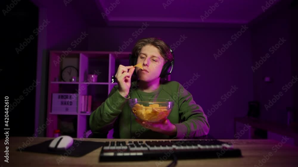 Portrait of a hungry gamer in casual clothes and headset having dinner ...