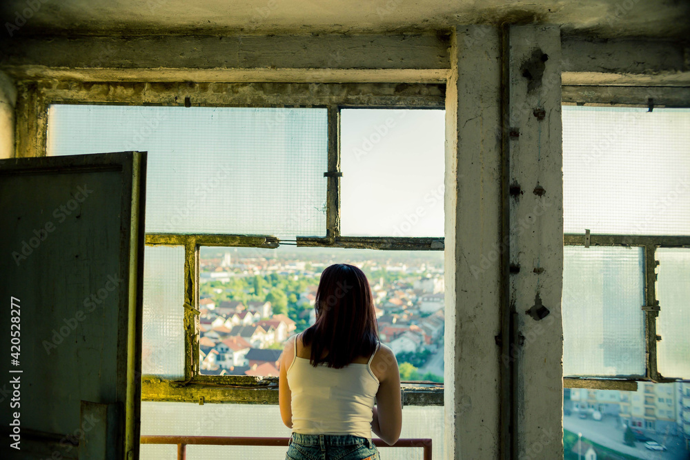 Back view of a female looking out of the window of an abandoned ...