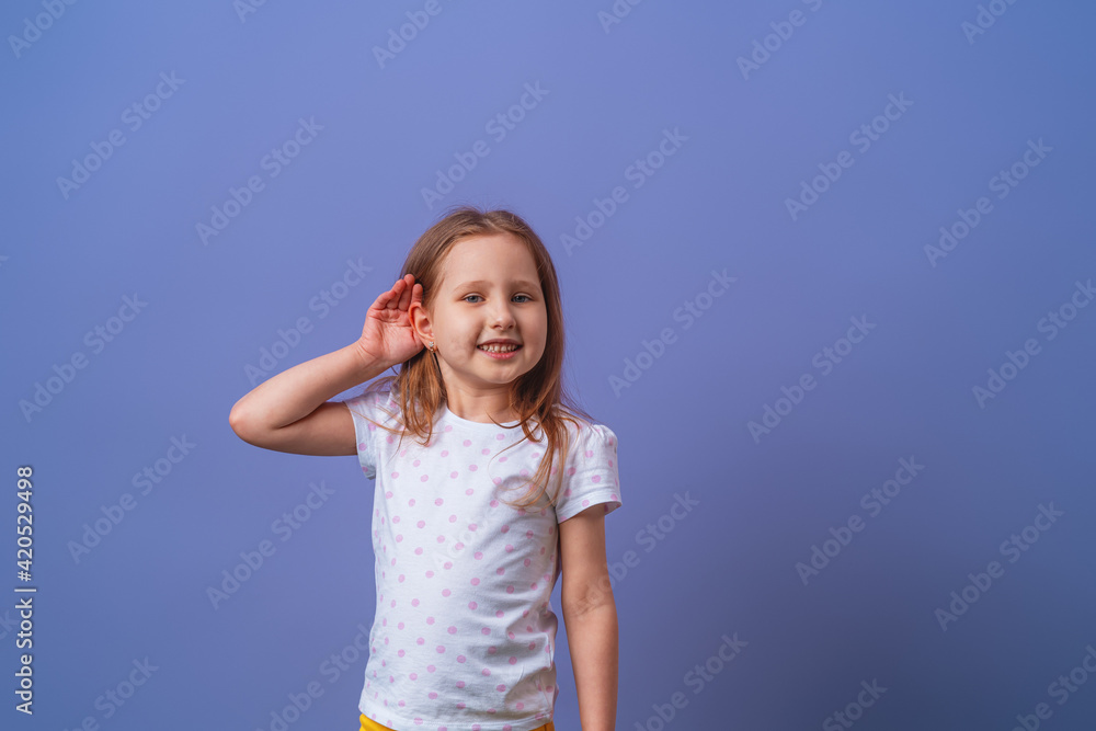 charming little girl smiles with her hand over her ear while listening ...