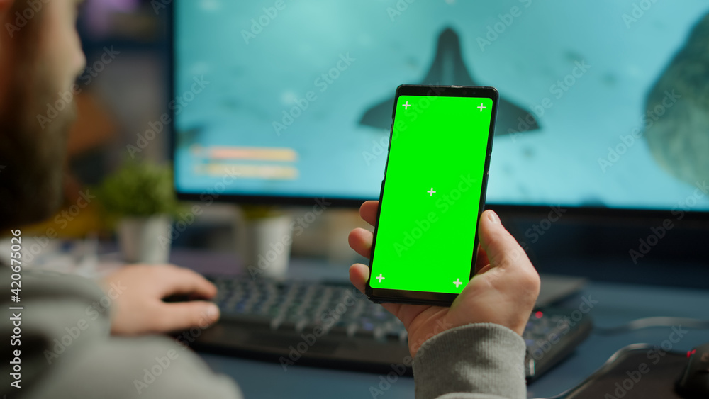 Competitive gamer looking at smartphone with green screen chroma key ...