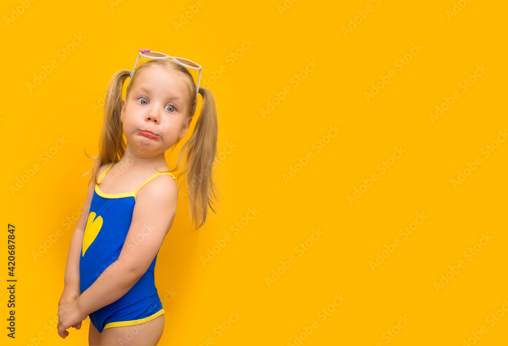 A naughty little girl makes faces and grimaces in a blue swimsuit on an ...