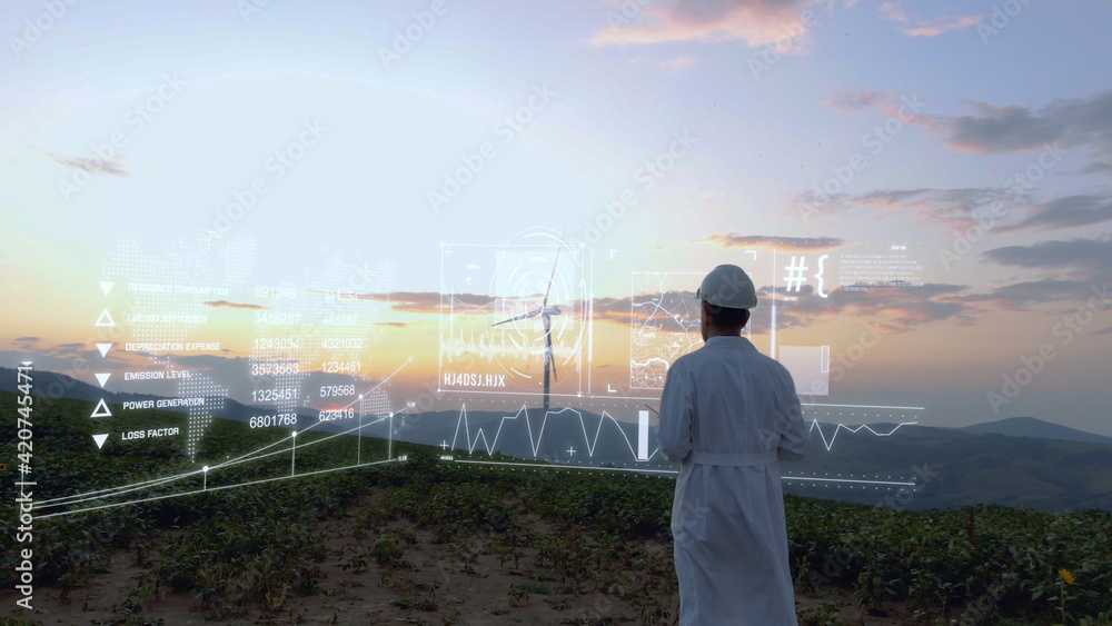 Engineer in white uniform working on wind farm on sunset using ...