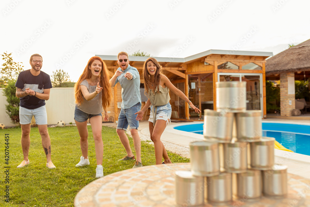 Man throwing a ball knocking down pyramid of tin cans while at a party ...