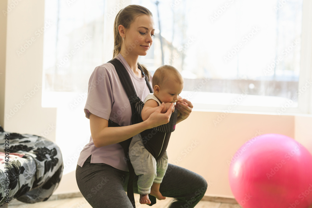 A young mother performs sports exercises squats and lunges with the ...