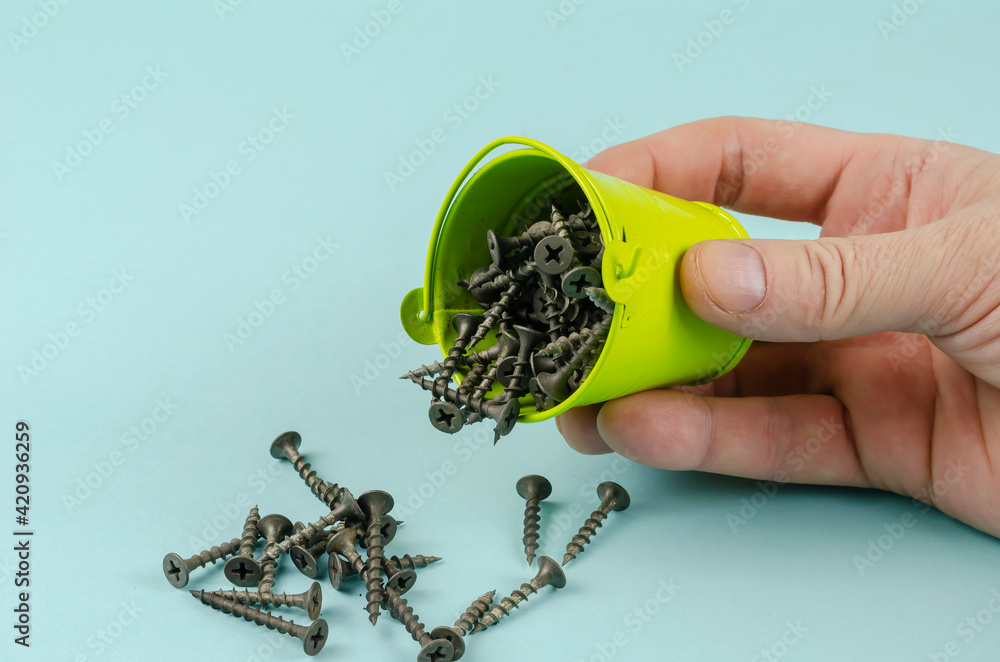 Screws, a hand and a small green bucket on a light blue backgrou Stock ...