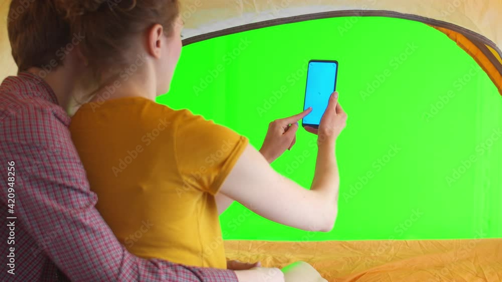 Couple sits hugging in a tent and uses phone, greenscreen. Man and ...