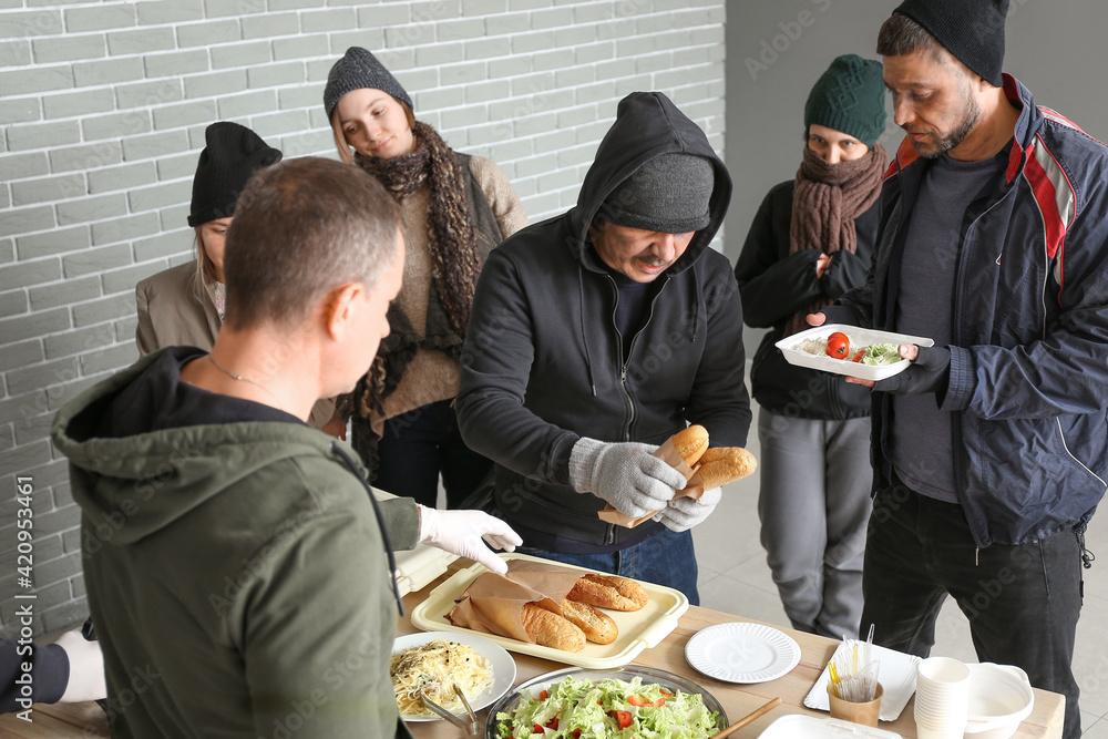 Foto de Volunteer giving food to homeless people in warming center do ...