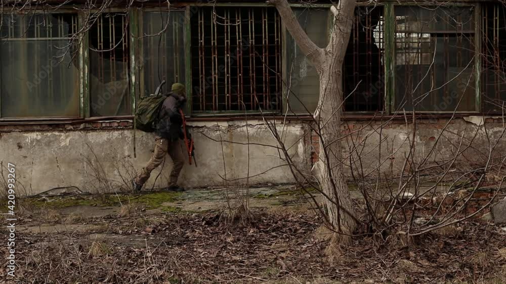 A man with a rifle in his hands and a backpack behind him moves through ...