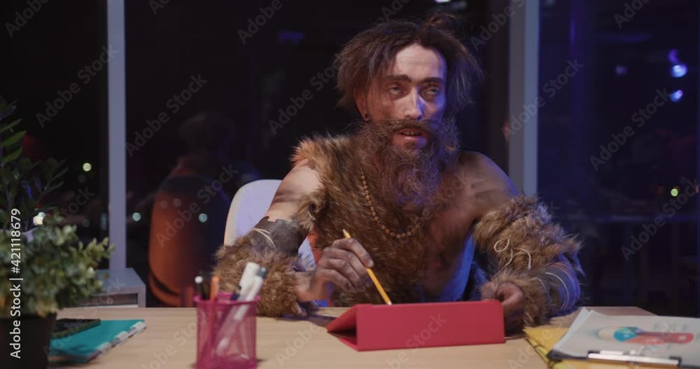 Nomadic tribal caveman in furty animal clothes sitting at table ...
