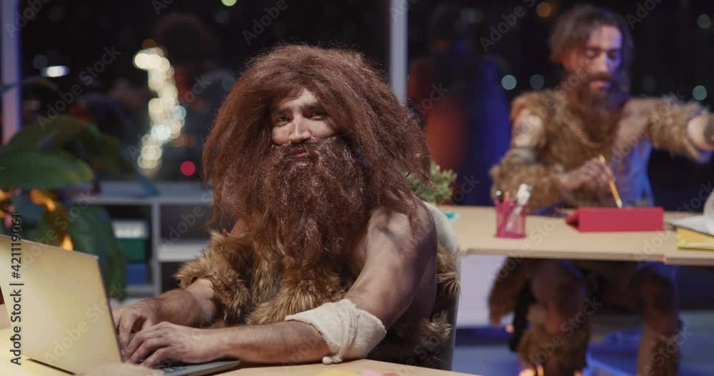 Funny neanderthal caveman in furry clothes using laptop with colleague ...