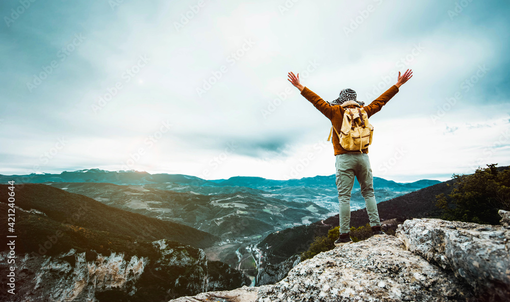 Man standing on edge of mountain feeling victorious with arms up in the ...