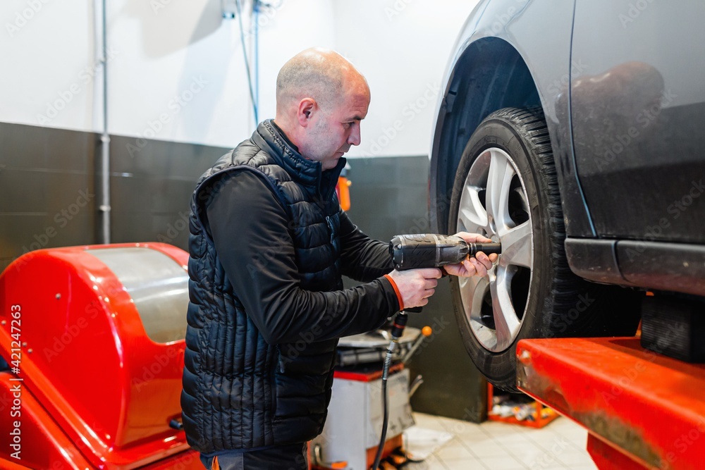 Mechanic in a car repair shop putting a wheel on a vehicle on an ...