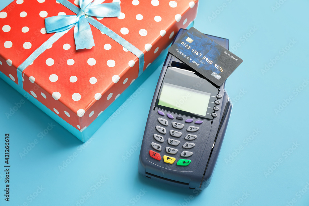 Payment terminal with credit card and gift box on color background ...