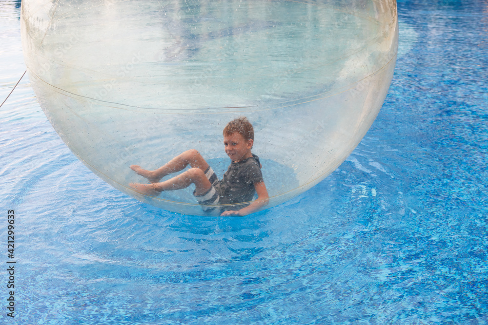 Little boy have fun inside big plastic balloon on the water of swimming ...