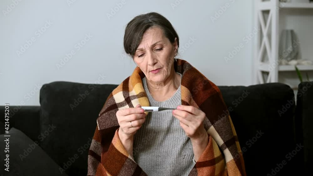 An older lady measures body temperature with a thermometer. Sick senior ...