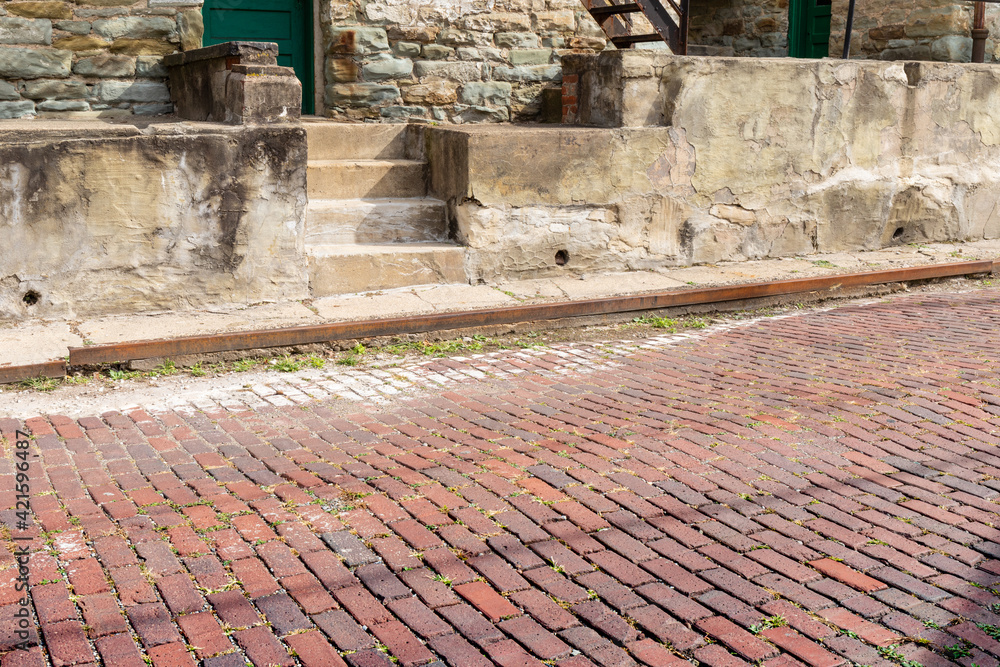 Brick street beside a narrow sidewalk, curb of rusted metal, crumbling ...