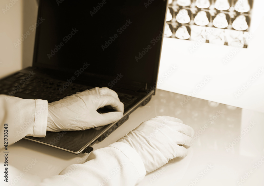 Doctor sits in front of laptop, computer monitor and examines MRI ...