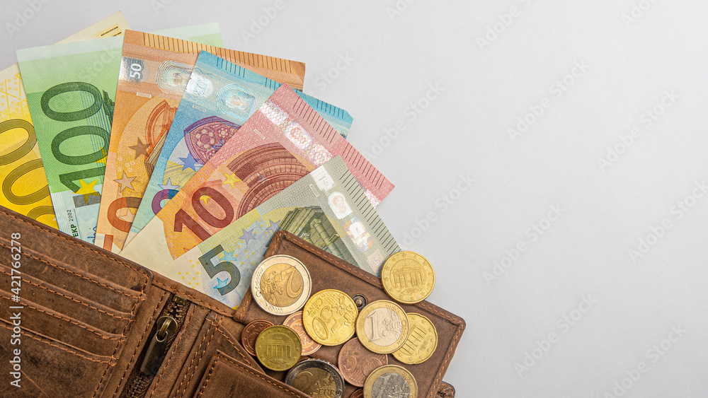 Euromünzen und Banknoten und Porte­mon­naie liegen auf einem wießen ...