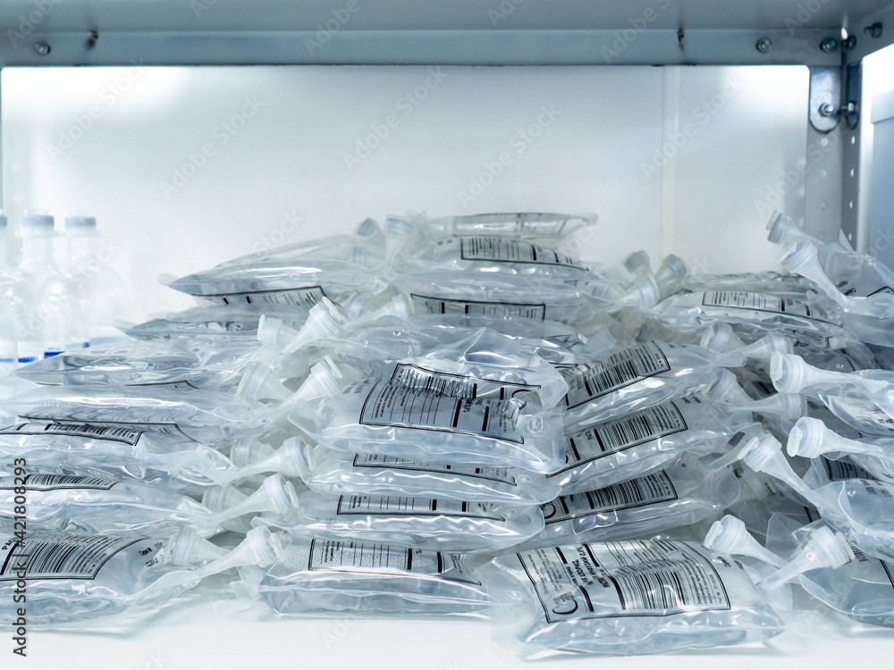 A large pile of intravenous saline bags in a hospital on a rack. The ...