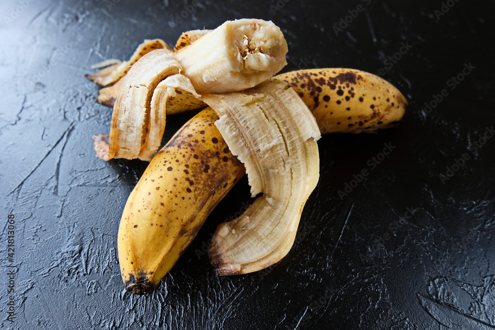 Overripe bananas with dark spots on the skin on black background. One ...