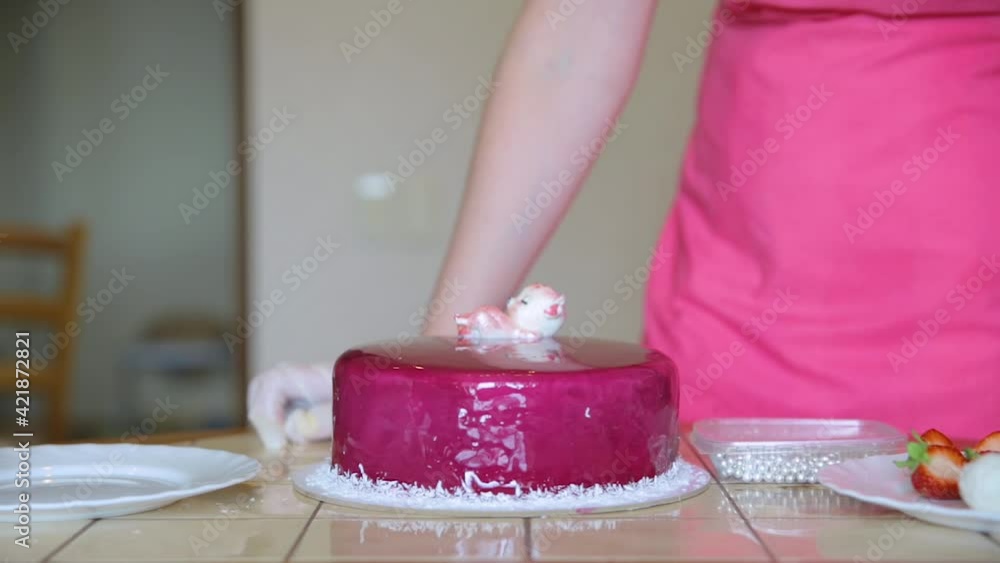 A female hand in a glove decorates a mousse cake with pink icing with a ...