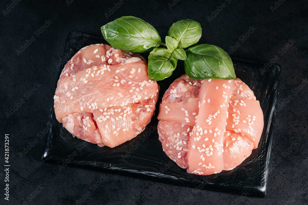 Raw chicken burger with basil leaves and spices on a black background ...