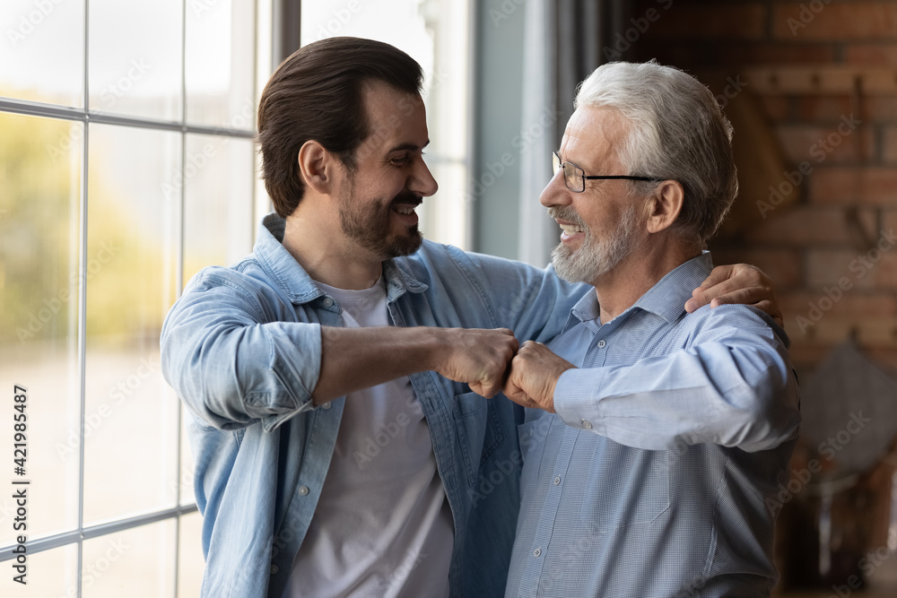 Overjoyed mature Caucasian 60s father and grownup son give fists bump for shared goal. Happy ...