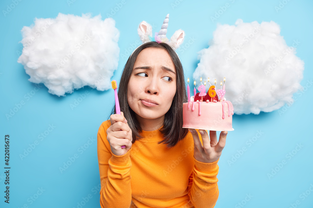 Upset Asian woman looks sadly at cake holds toothbrush has caries after ...