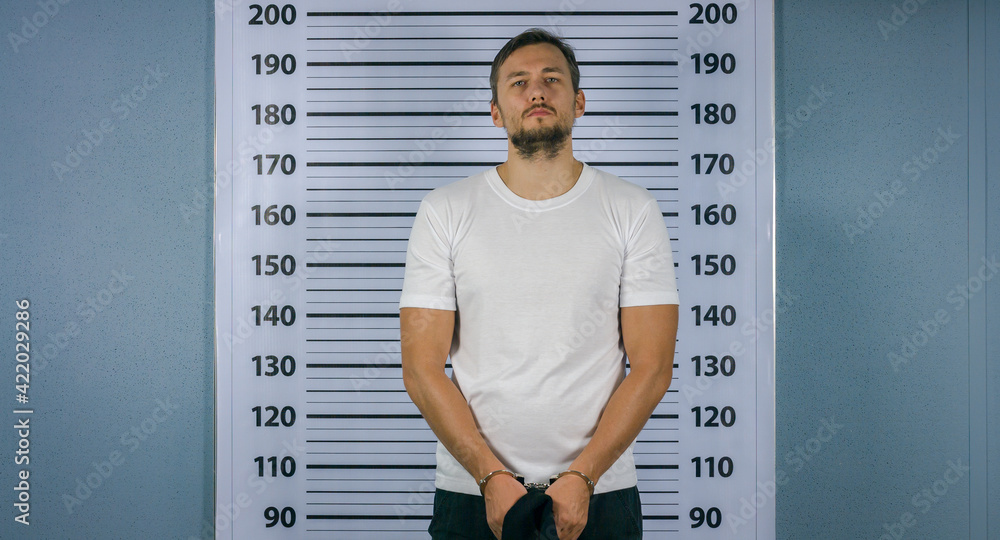 Arrested a man in handcuffs standing near a white board with a scale ...