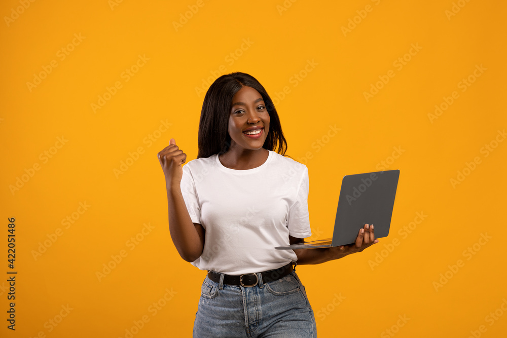 Smiling young black woman holding laptop and raising fist up Stock ...