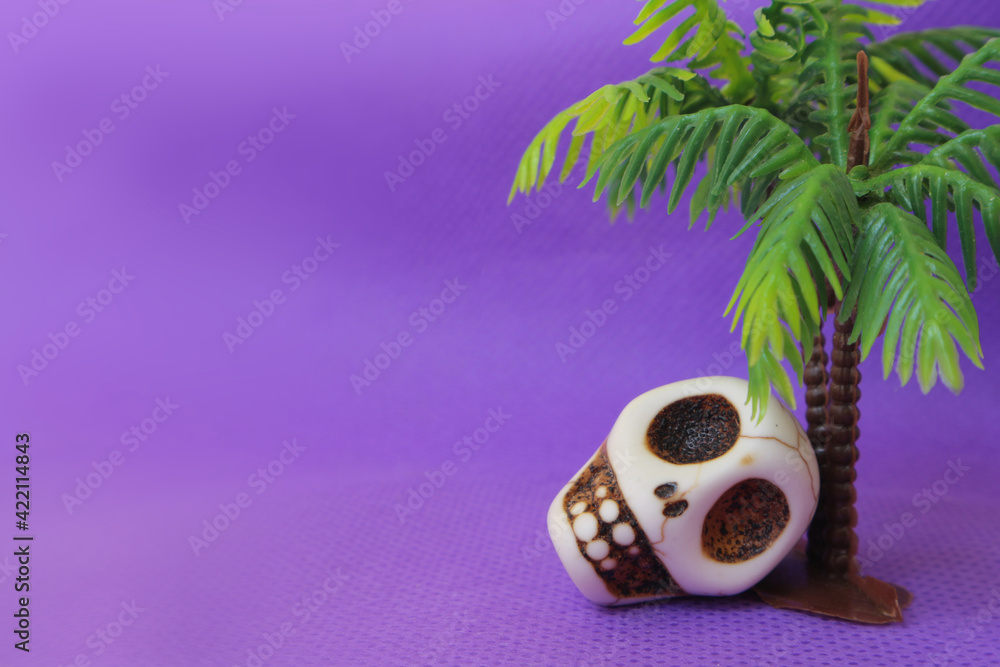Toy human skull under a palm tree on a bright violet background. Stock ...